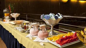 Uma mesa de buffet com diversos alimentos e bebidas, incluindo frutas, sanduíches e sucos em jarras.