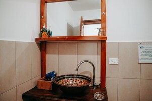 Um banheiro com toucador de madeira, pia decorativa e espelho em cima.