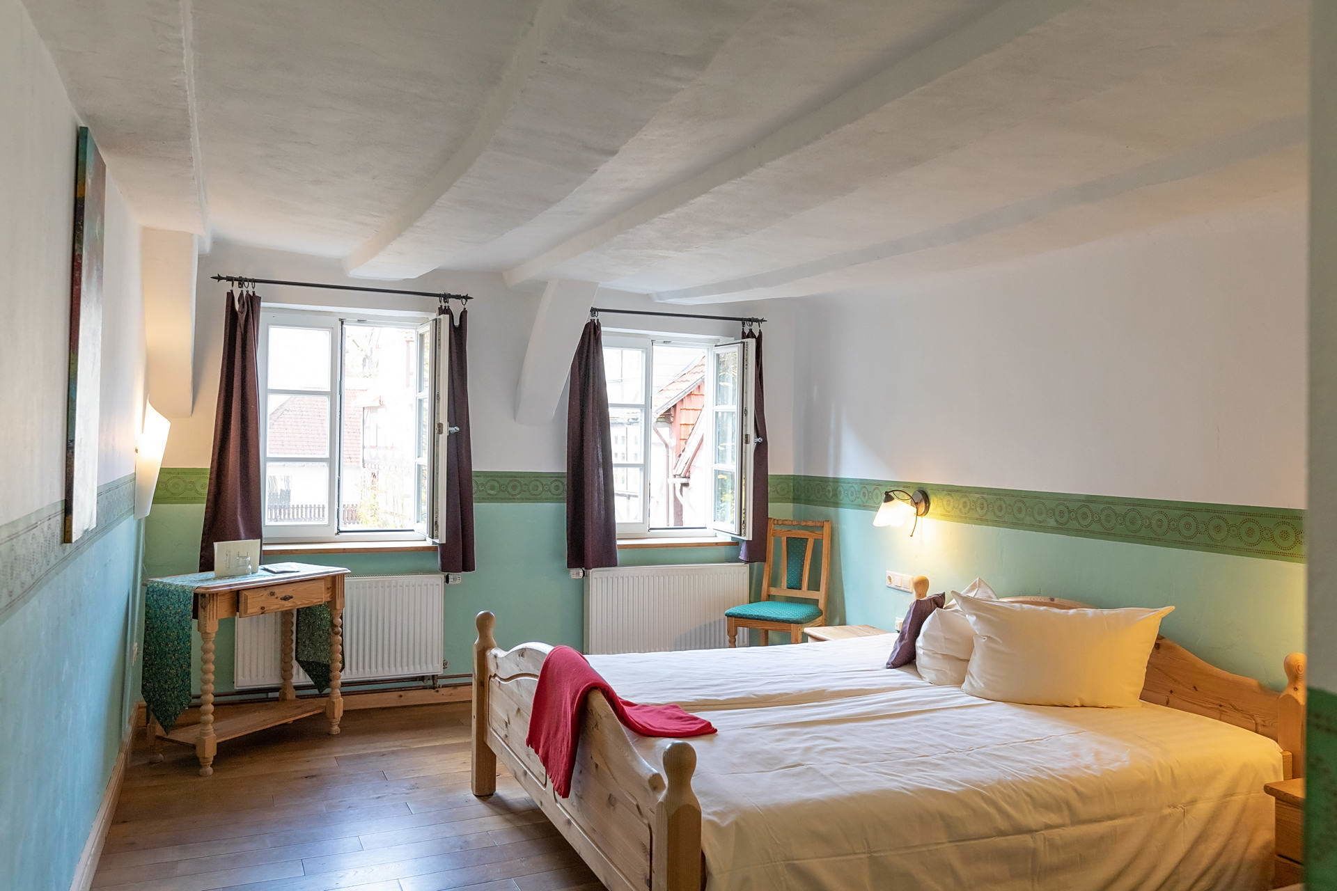 Um quarto com uma cama, uma cadeira, uma mesa e uma janela com cortinas.
