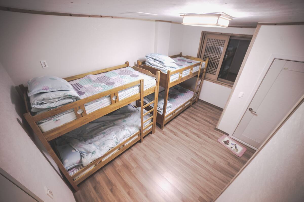 Quarto com três beliches, piso de madeira, porta e janela com padrão quadriculado.