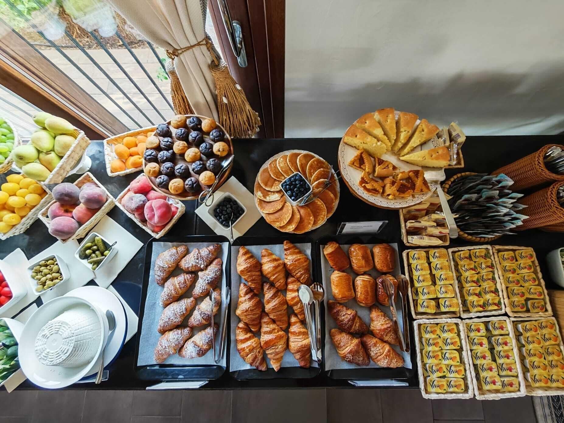 Mesa de buffet com diversos alimentos, incluindo frutas, doces e sobremesas.