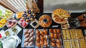 Mesa de buffet com diversos alimentos, incluindo frutas, doces e sobremesas.