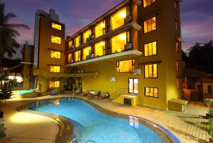 Hotel com piscina, várias varandas e um céu ao pôr do sol.