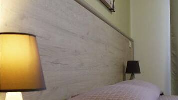 Quarto de hotel com cabeceira de madeira, mesa de cabeceira com abajur, cama com colcha rosa e quadro pendurado na parede.