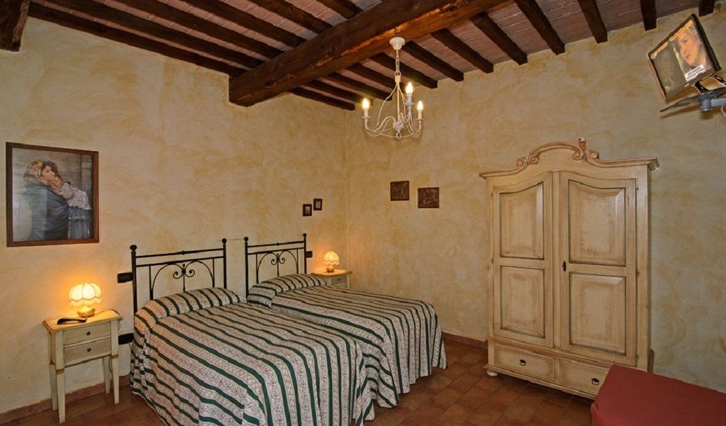 Quarto com cama de casal, mesas de cabeceira com luminárias, guarda-roupa e um candelabro.