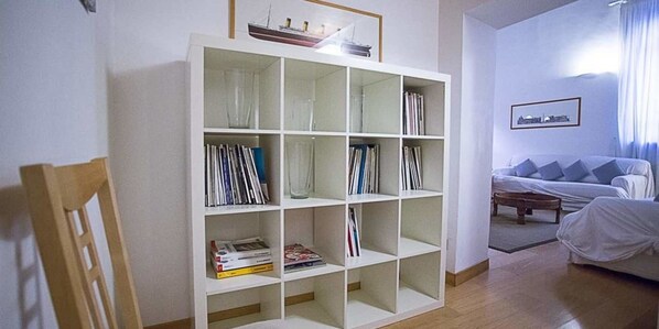 Uma sala de estar com uma estante branca, uma cadeira de madeira, um sofá e uma moldura na parede.