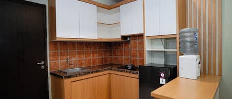 Uma cozinha compacta com armários de madeira, uma geladeira preta, um bebedouro e um painel de azulejos.