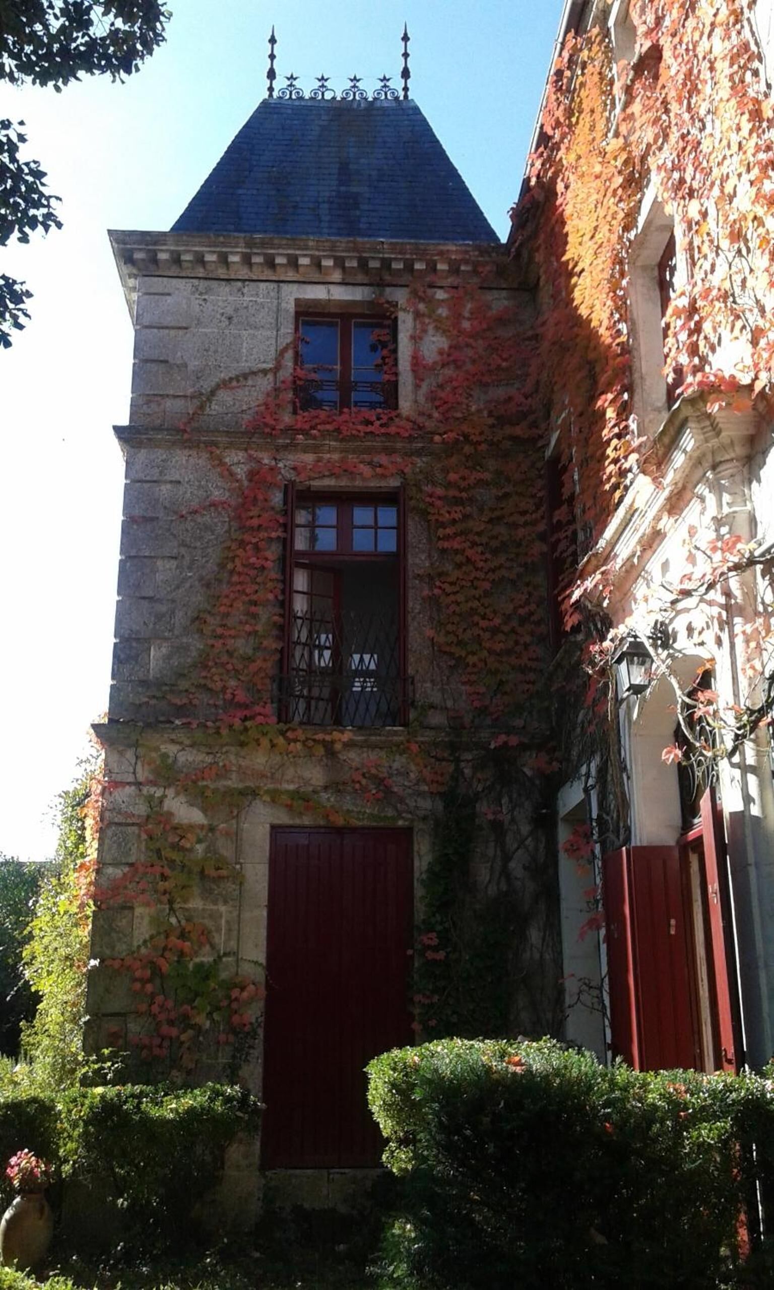 Um edifício de pedra com porta e janelas vermelhas, coberto por hera vermelha.