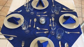 Mesa de jantar posta para seis pessoas, com guardanapos azuis, pratos brancos e talheres.