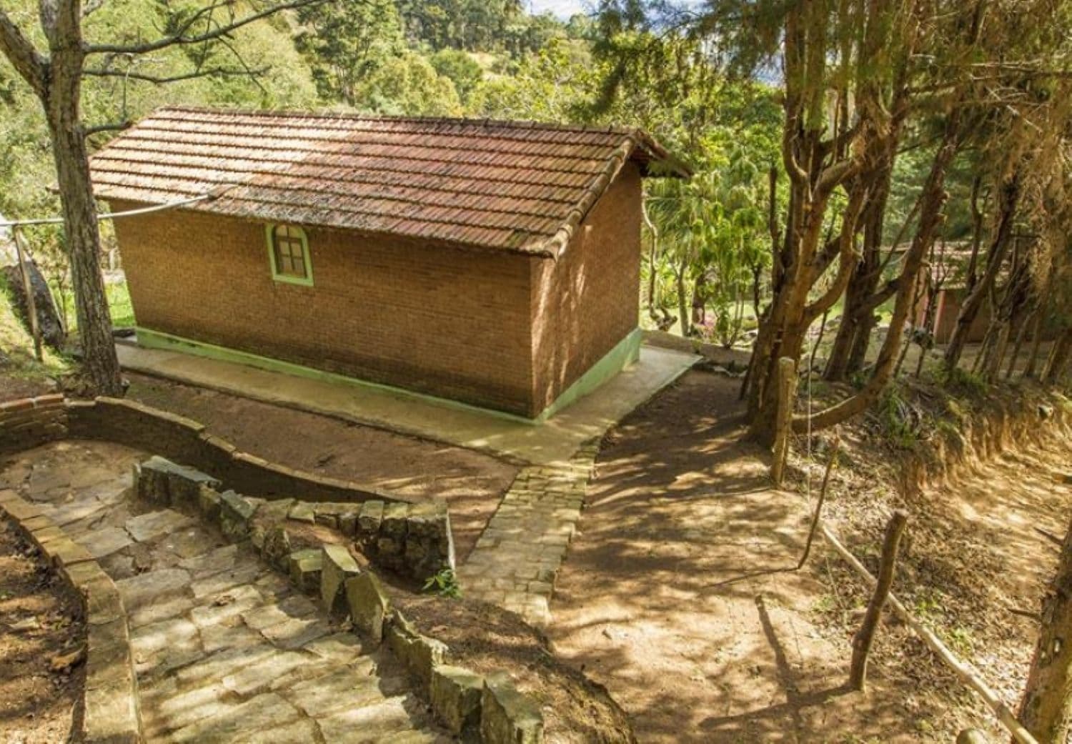 Um edifício rústico de tijolos com telhado de cerâmica, rodeado por árvores e um caminho de pedra que leva a ele.