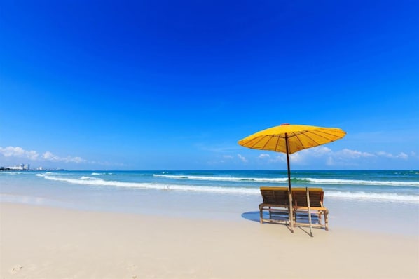 Uma praia com um banco de madeira e um guarda-sol amarelo.