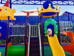 Uma área de recreação infantil com escorrega, rede de escalada e estrutura de jogos com coroa e figuras de animais.