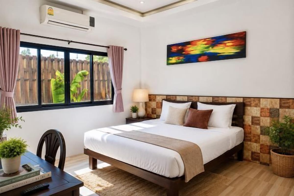 Quarto com cama, escrivaninha, cadeira, janela com cortinas, quadro e planta em vaso.