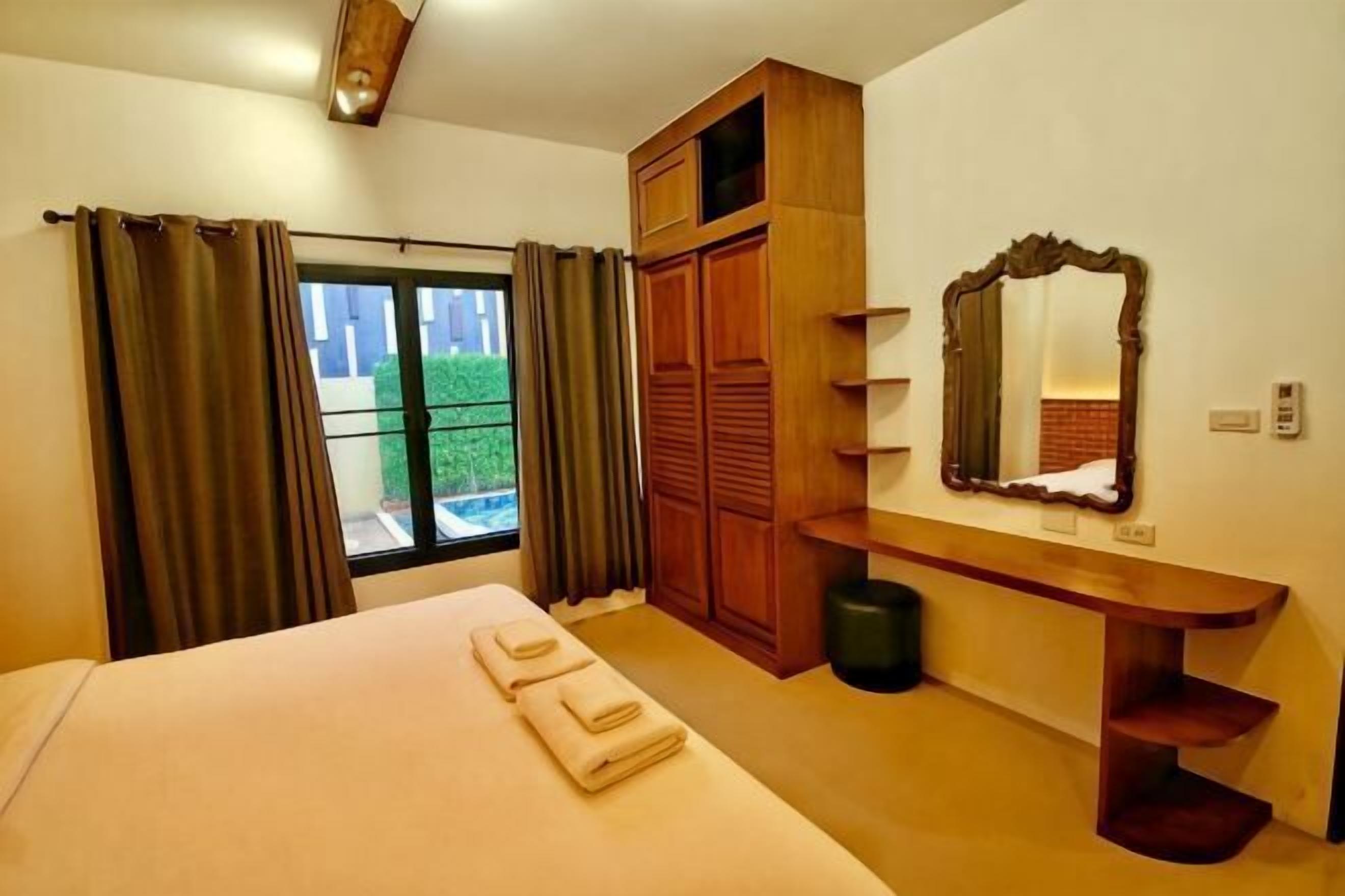 Quarto com cama, guarda-roupa de madeira, espelho e janela com cortinas.