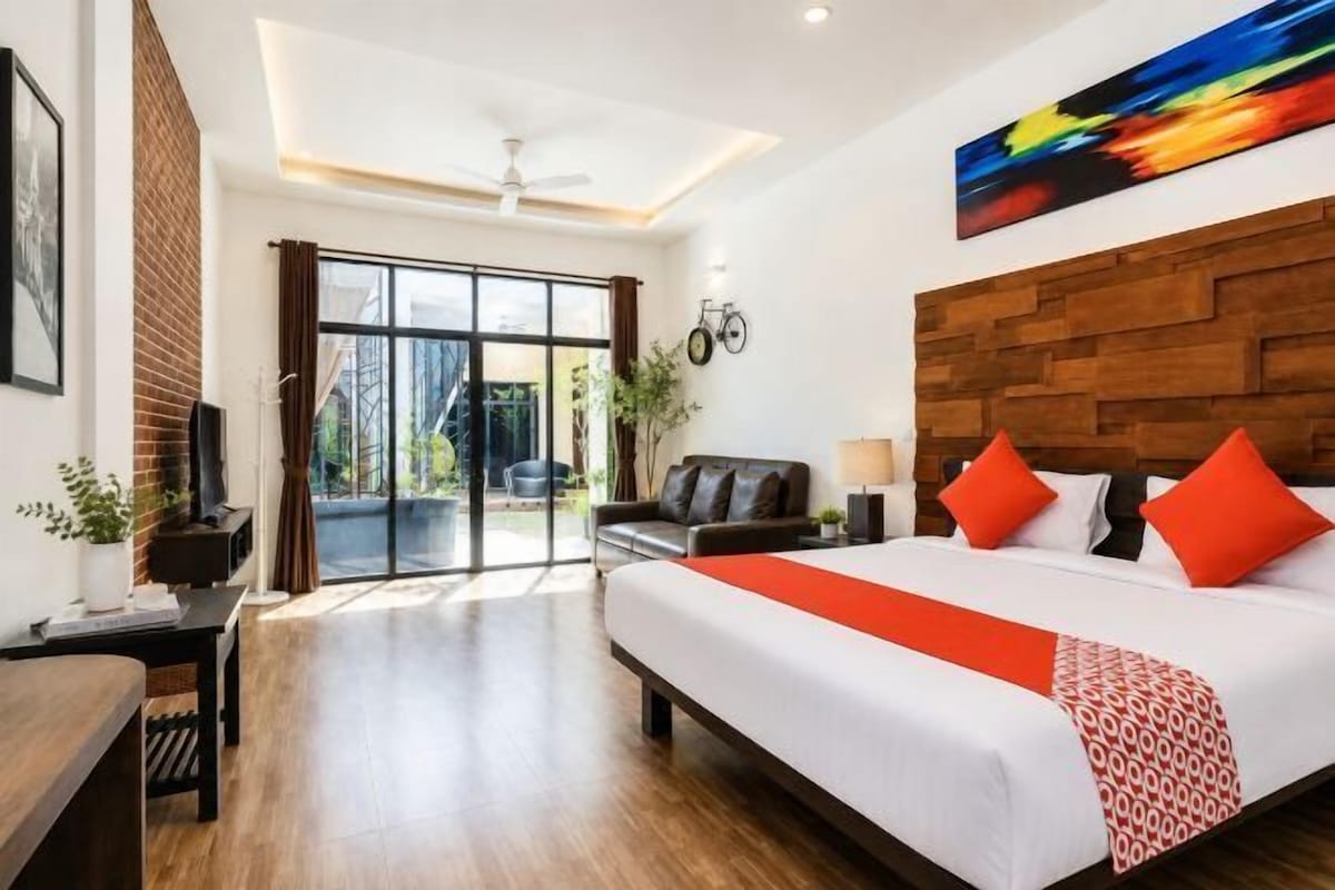 Quarto de hotel com uma cama grande, uma escrivaninha, uma cadeira, uma TV e uma porta de vidro que dá para uma área externa.