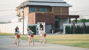 Três pessoas andando de bicicleta em um caminho pavimentado, em frente a uma casa moderna com telhado inclinado e grandes janelas.