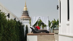 Varanda com espreguiçadeira e toldo, com vista para um templo com andaimes.
