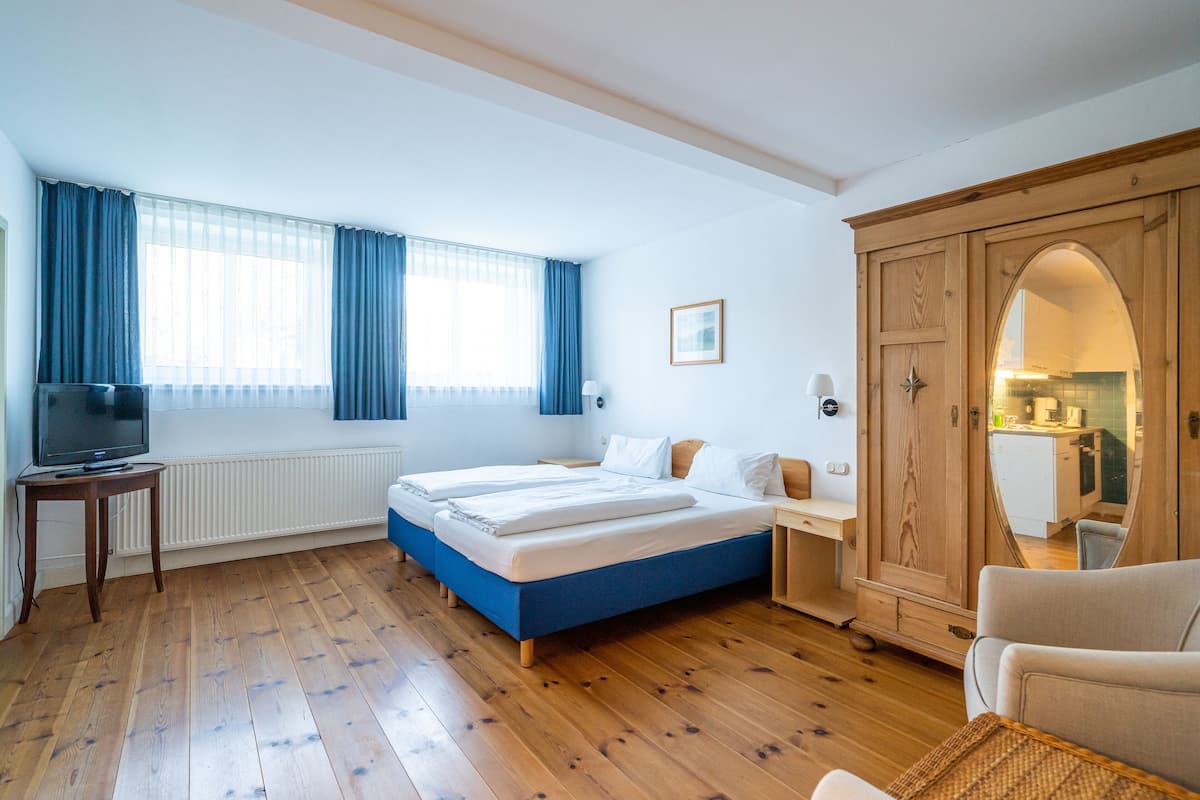Quarto com piso de madeira, uma cama, televisão em uma mesinha de cabeceira e um guarda-roupa com espelho.