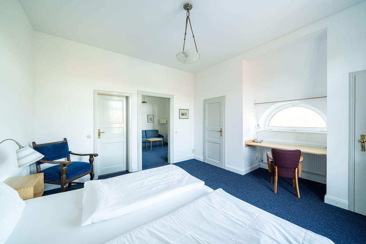 Quarto de hotel com cama, escrivaninha, cadeira e janela.