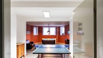 Um quarto com mesa de pingue-pongue, mesa de bilhar e suporte para tacos de bilhar.