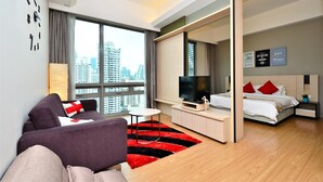 Quarto de hotel moderno com uma janela grande, um sofá, uma cama, uma televisão e uma escrivaninha.