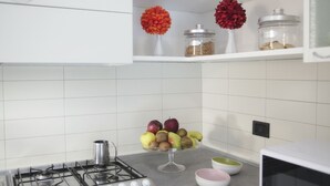 Cozinha com armários brancos, fogão a gás, tigela de frutas e flores decorativas.