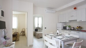 Cozinha moderna com armários brancos, uma mesa de jantar posta para quatro e um pequeno espaço de refeições com uma cadeira.