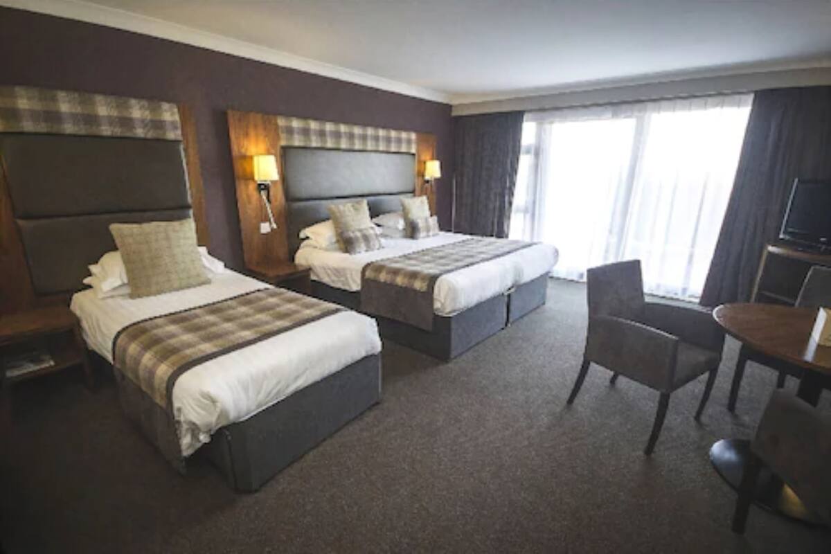 Quarto de hotel com duas camas, uma mesa e uma cadeira.