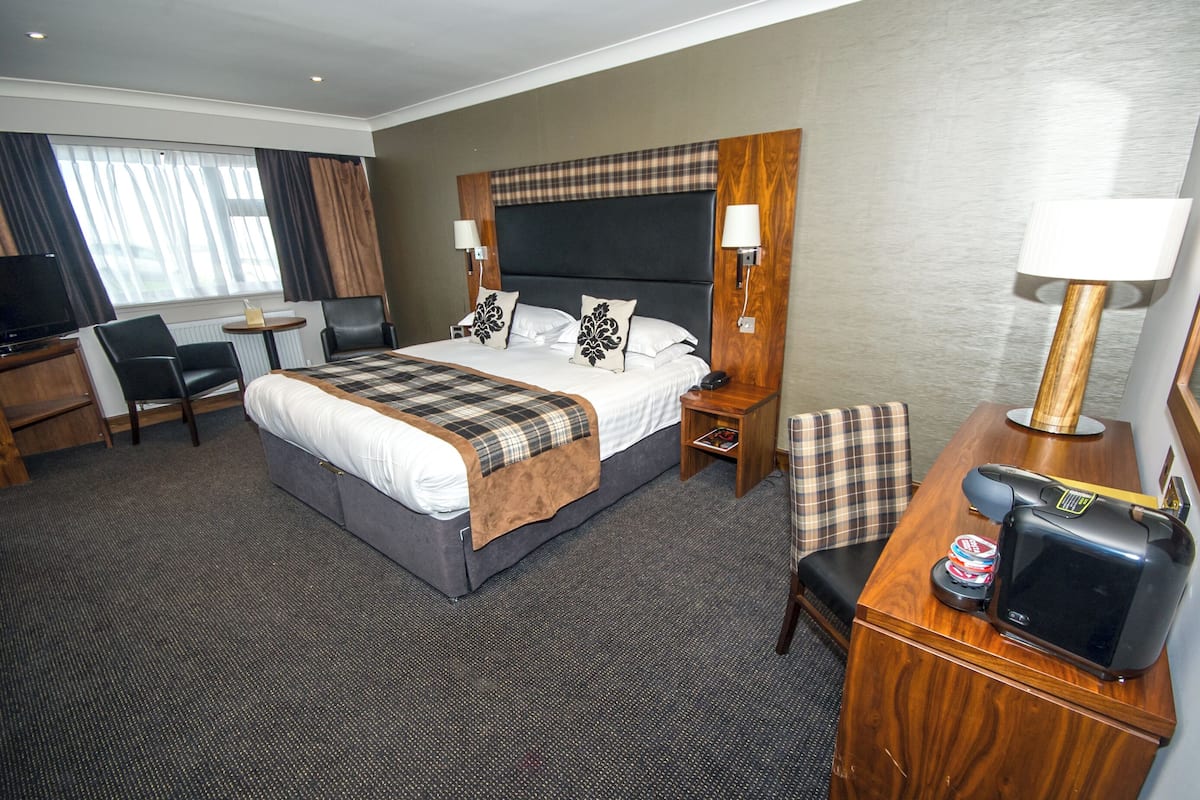 Quarto de hotel com uma cama grande, uma escrivaninha com computador, uma cadeira, uma TV e uma máquina de café.