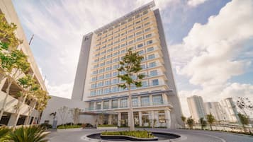 Um hotel moderno com um pátio central, vários andares e um 'R' bem visível na fachada.