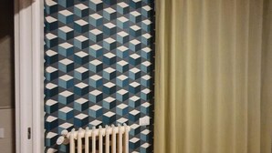 Um quarto com parede estampada, um radiador e uma janela com cortinas.