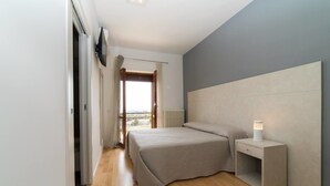 Quarto com cama, mesa de cabeceira e vista para o exterior.