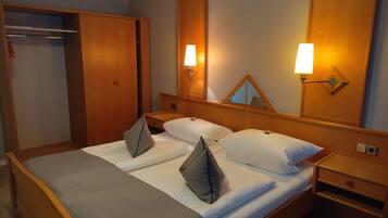Quarto de hotel com cama de casal, cabeceira de madeira, mesas de cabeceira, um guarda-roupa e luminárias fixadas na parede.
