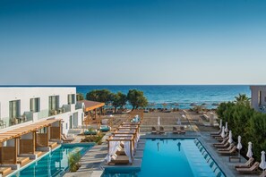Área de piscina em resort com espreguiçadeiras e guarda-sóis, vista clara do mar e praia ao fundo.