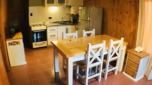 Uma cozinha compacta com armários brancos, uma mesa de jantar de madeira e uma geladeira.