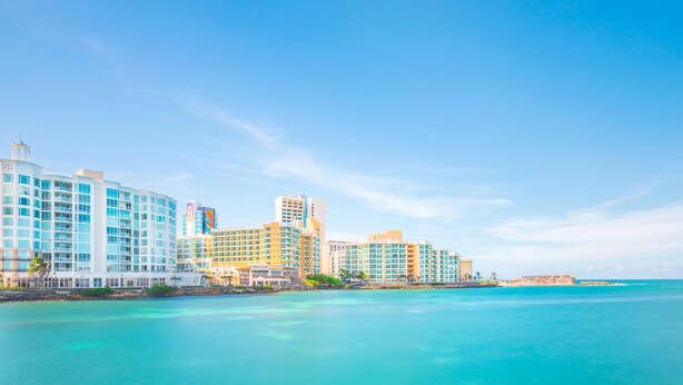 Um hotel à beira-mar com vários edifícios altos, um céu azul claro e águas turquesa.
