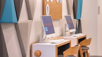 Uma área de recepção de hotel com duas estações de computador, uma mesa de madeira e um painel com placas de sinalização.