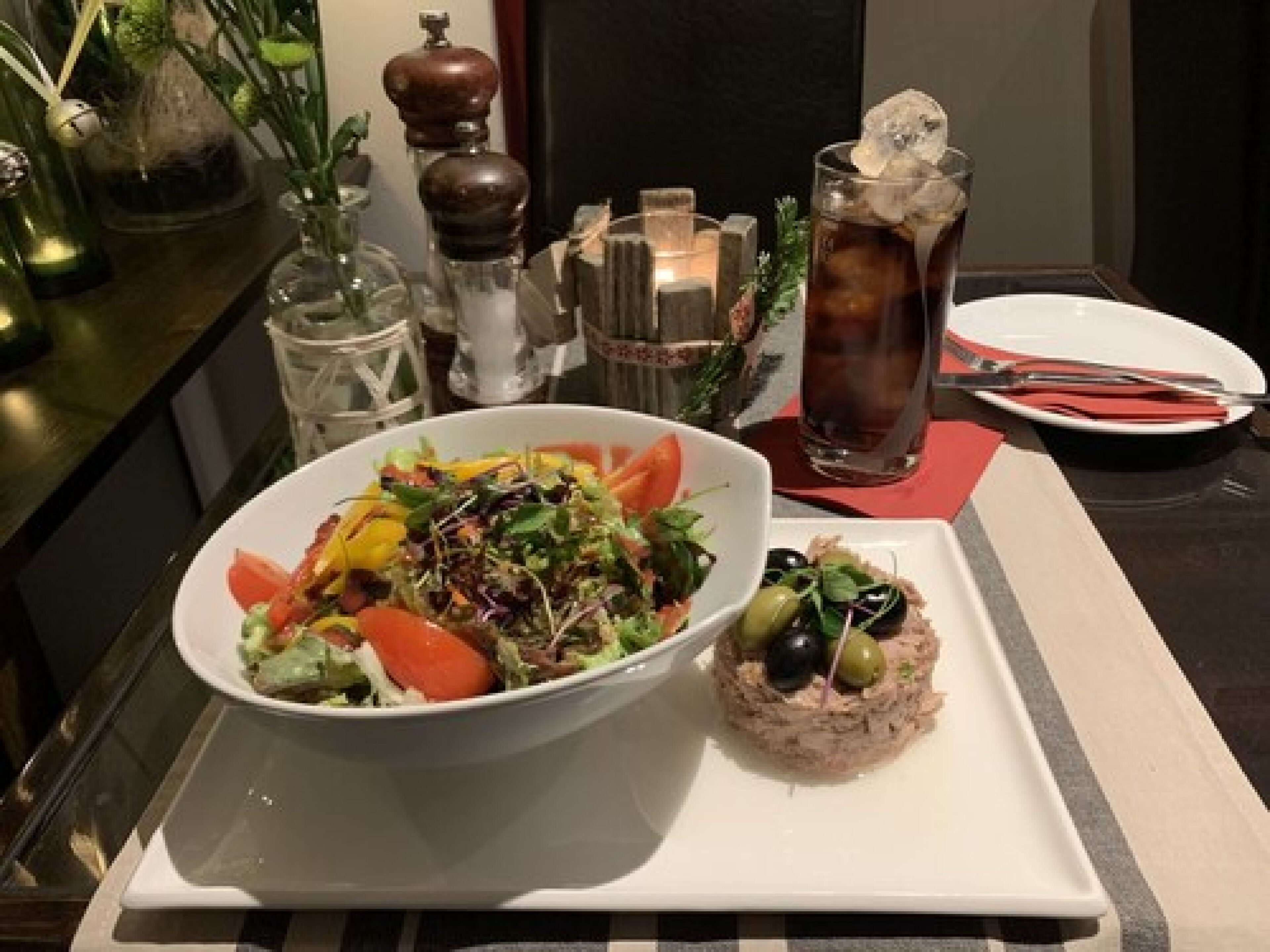 Uma mesa de jantar com uma salada, um prato de carne e uma bebida.