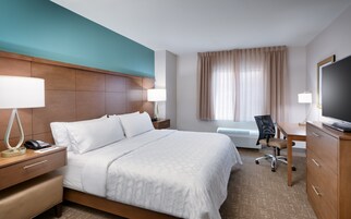 Quarto de hotel com cama, mesas de cabeceira, escrivaninha, cadeira, televisão e janela com cortinas.