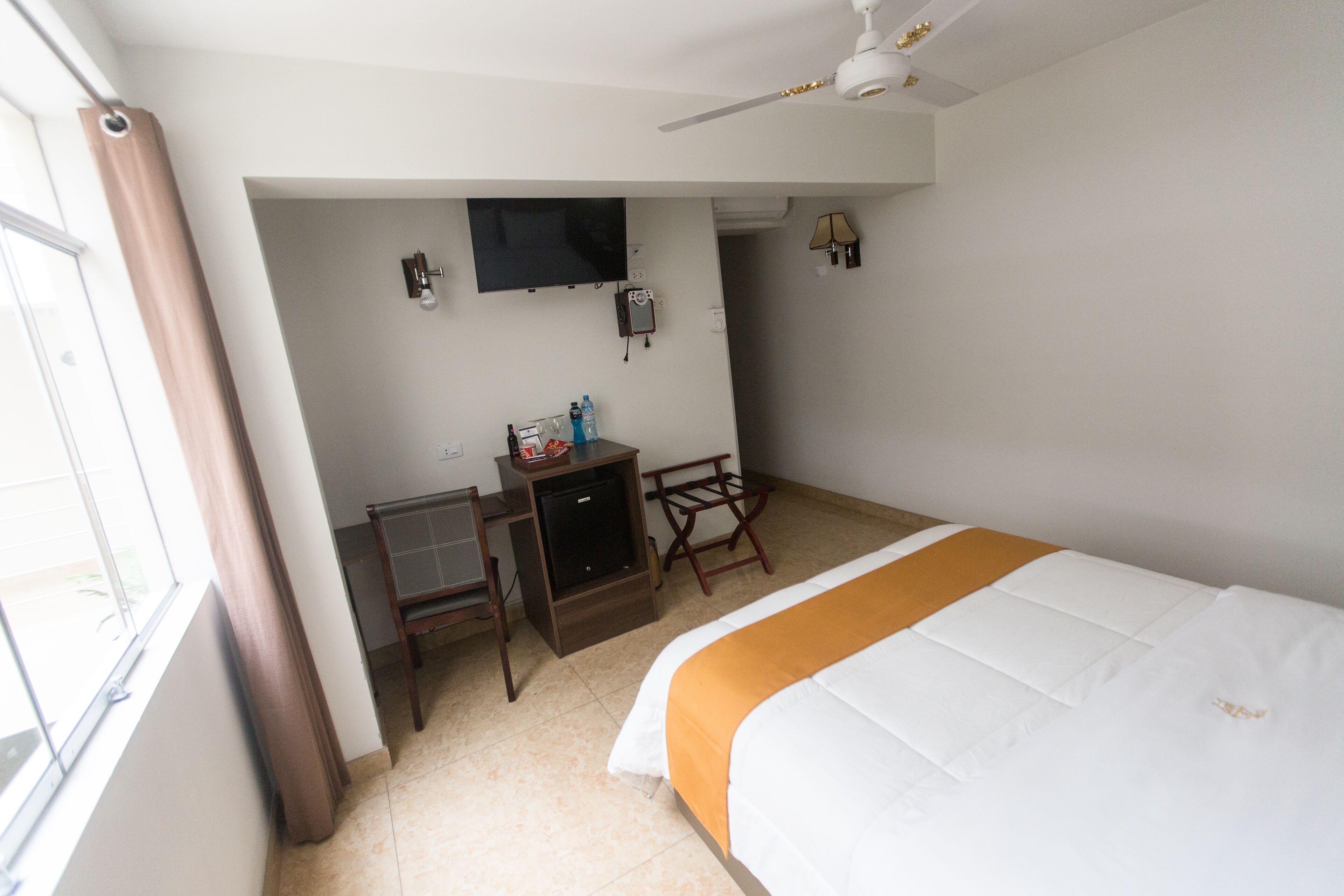 Quarto de hotel com cama, escrivaninha, televisão e ventilador de teto.