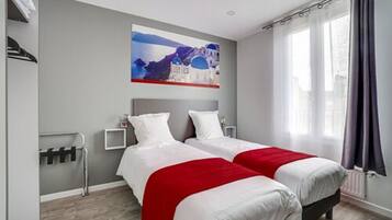 Quarto de hotel com duas camas, colcha vermelha e branca, pintura de uma paisagem costeira e uma janela com cortinas.