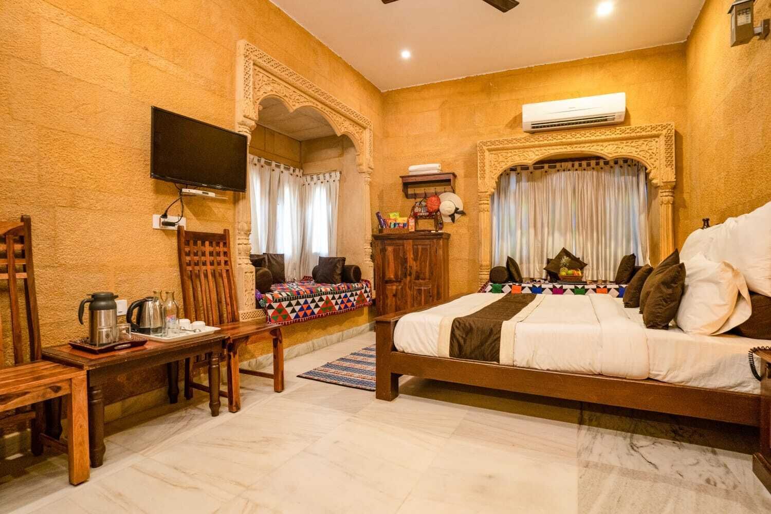 Quarto de hotel com cama, televisão, escrivaninha de madeira e um arco decorativo na parede.