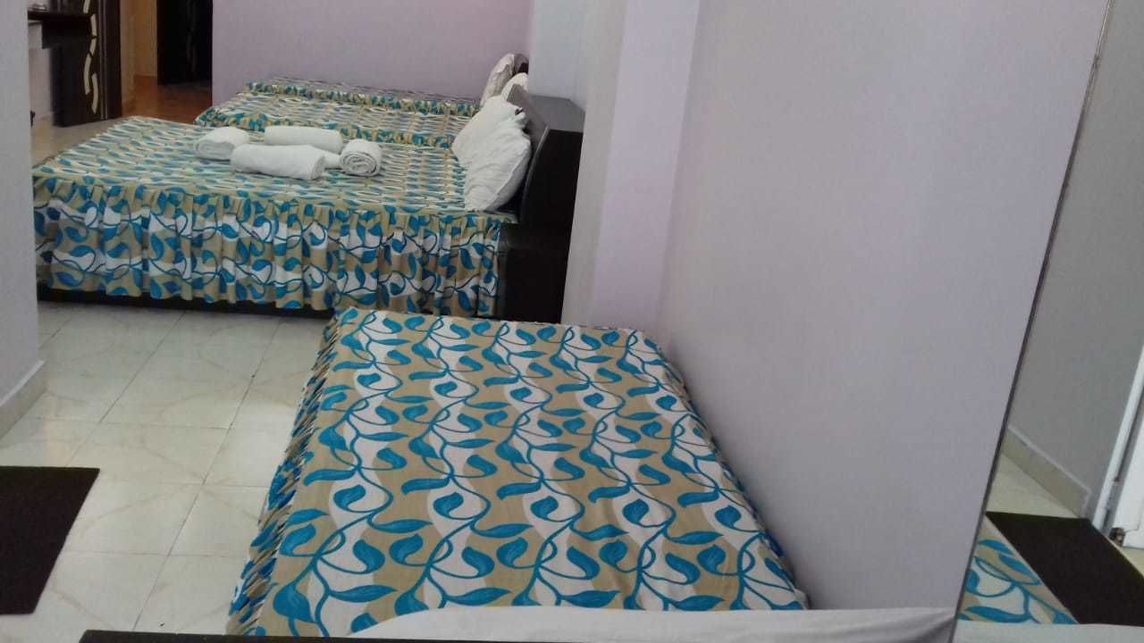 Quarto de hotel com duas camas, cada uma com colcha estampada. Há uma pequena mesa e uma cadeira no quarto.