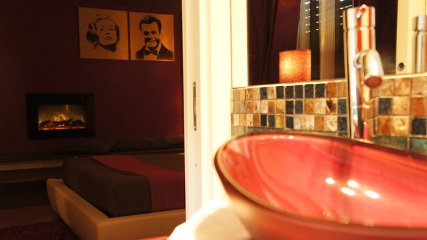 Casa de banho com lavatório vermelho, espelho e painel de azulejos.