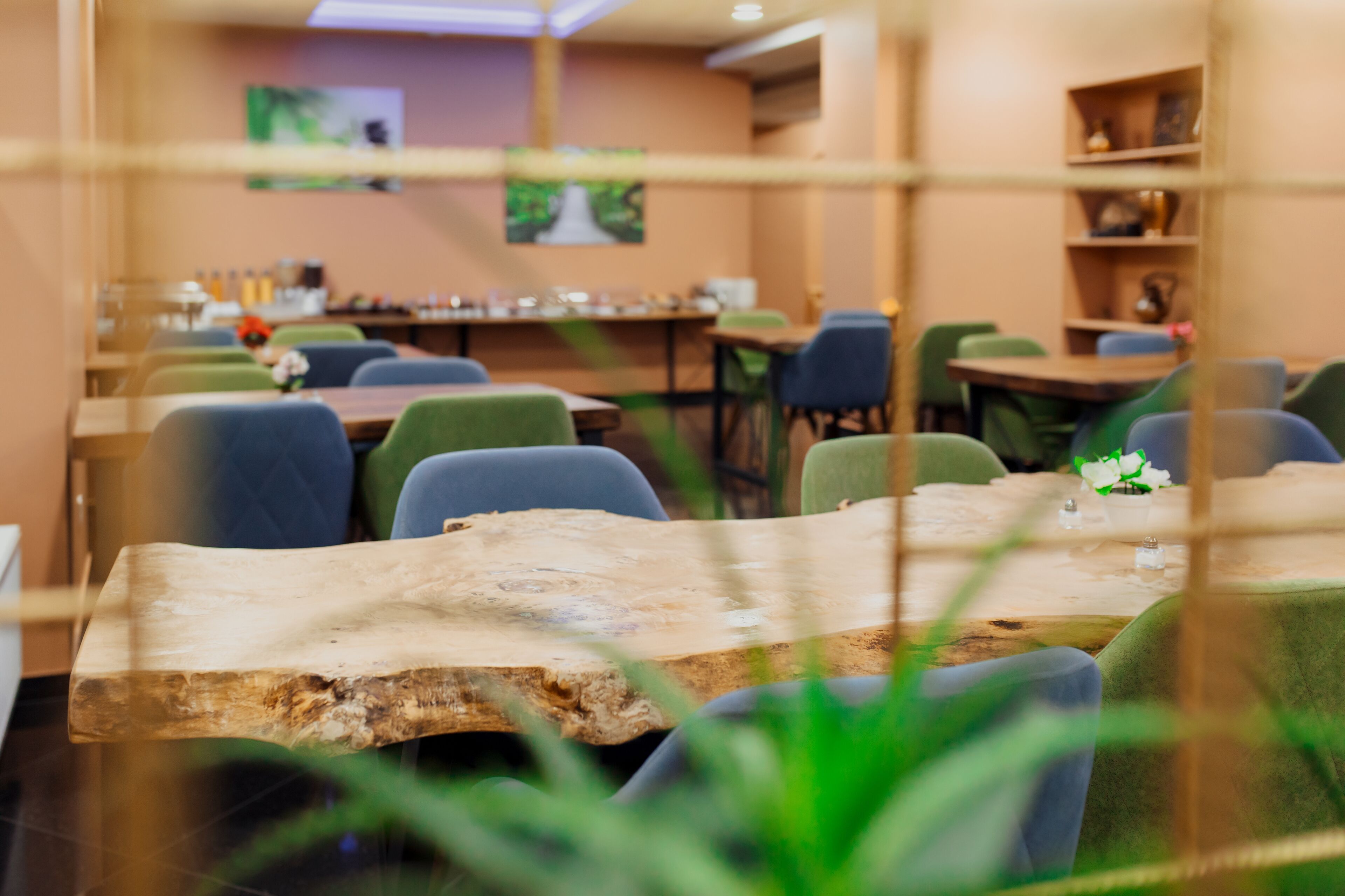 Restaurante com toalha de mesa rústica em madeira, cadeiras estofadas verdes e diversas mesas de jantar.