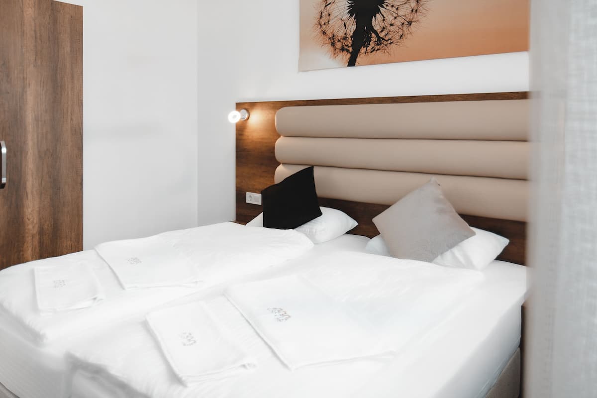 Cama bem arrumada com lençóis brancos e cabeceira com acabamento em madeira.