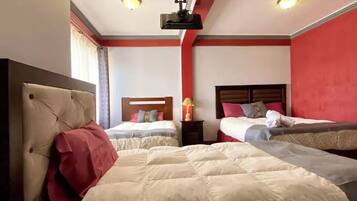 Quarto de hotel com duas camas, uma parede de destaque vermelha e projetor instalado no teto.