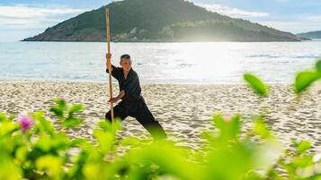 Uma pessoa praticando artes marciais numa praia arenosa, com montanhas ao fundo.