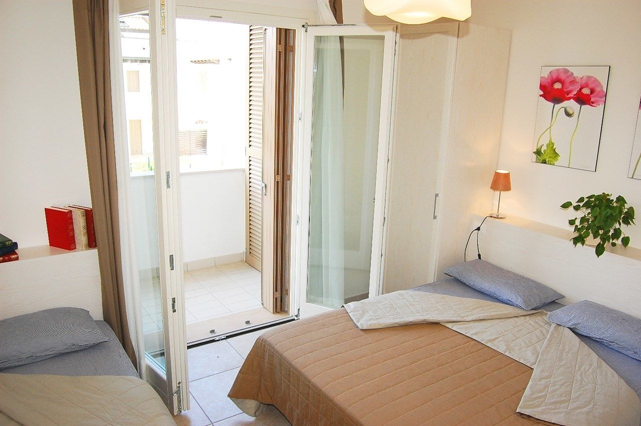 Quarto com duas camas, uma porta de correr de vidro para uma varanda, luminária de cabeceira e um quadro de flores na parede.
