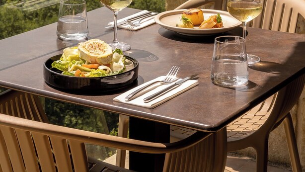 Mesa posta com salada, dois copos de vinho branco e um prato de comida, com vista para uma paisagem deslumbrante.